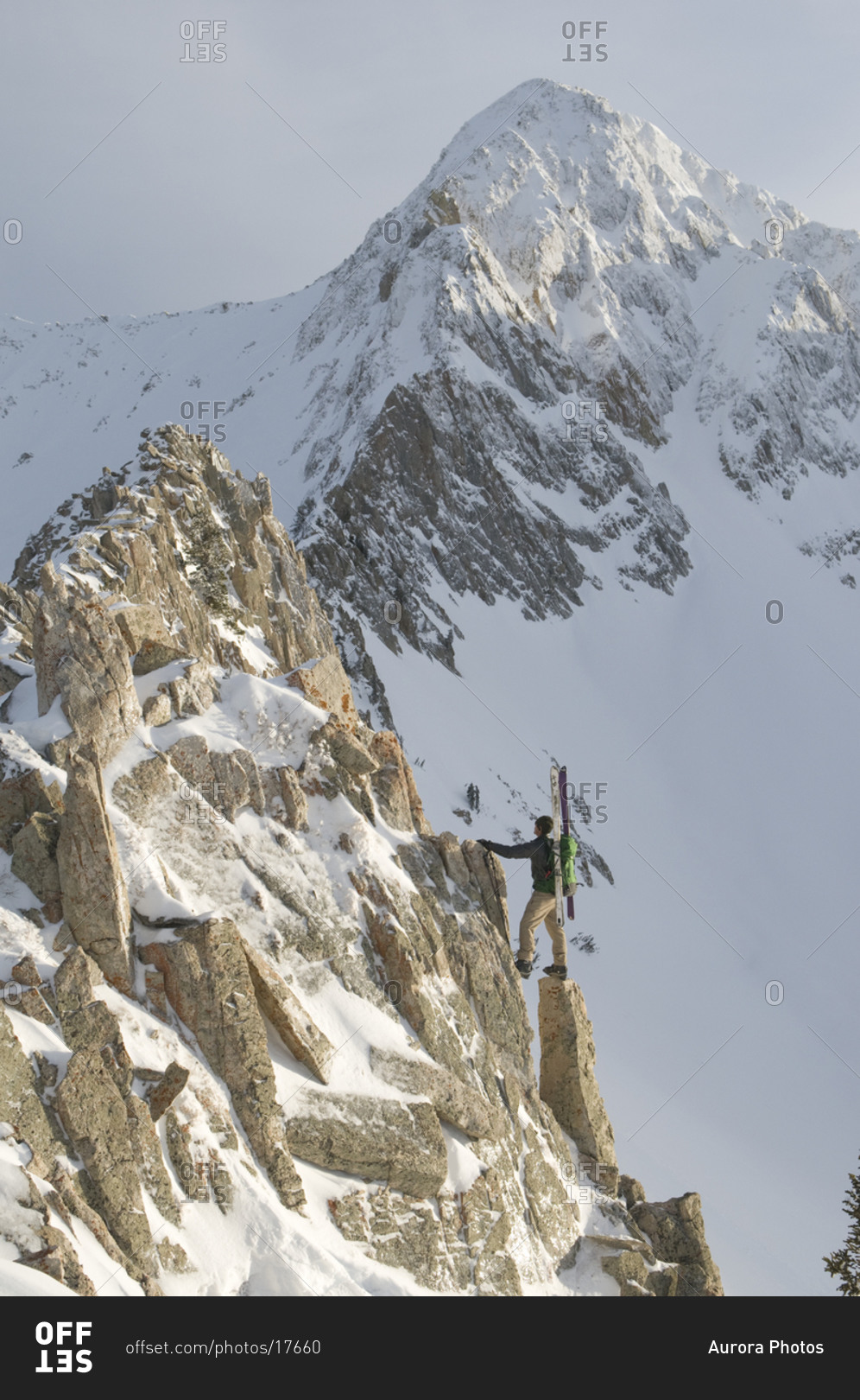 A man on a rocky ridge with skis below snowy mountain, Red Pine Canyon ...