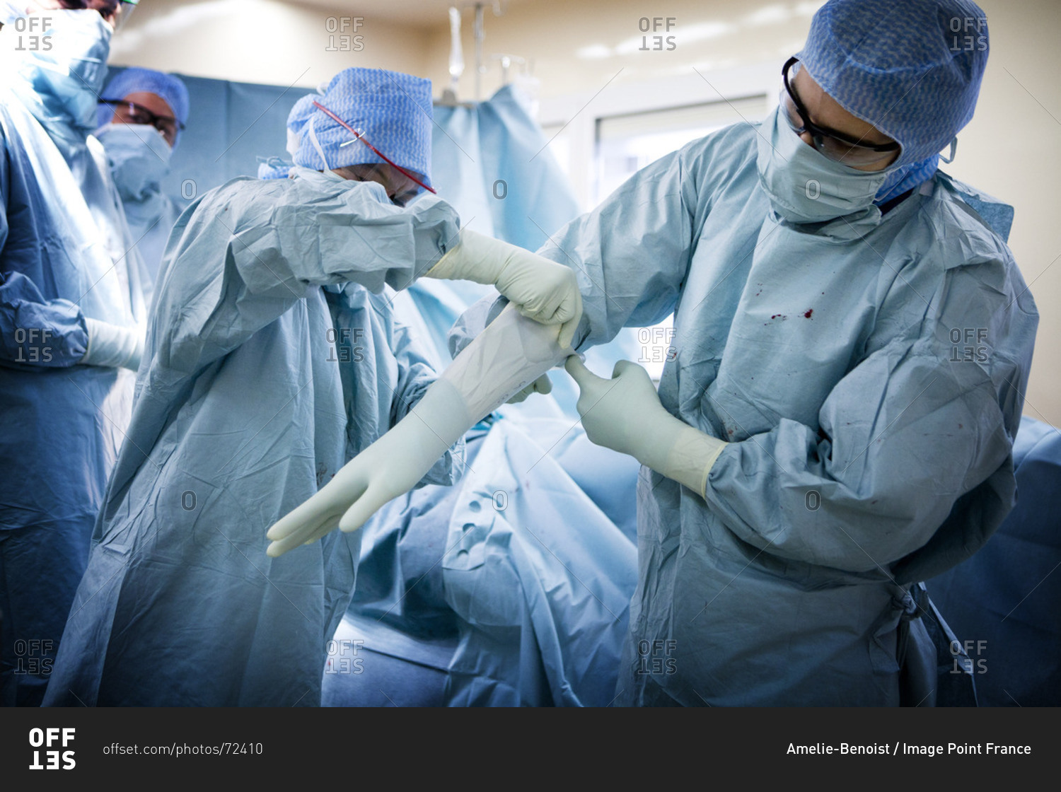 Doctor helping surgeon put on gloves in operating room stock photo - OFFSET