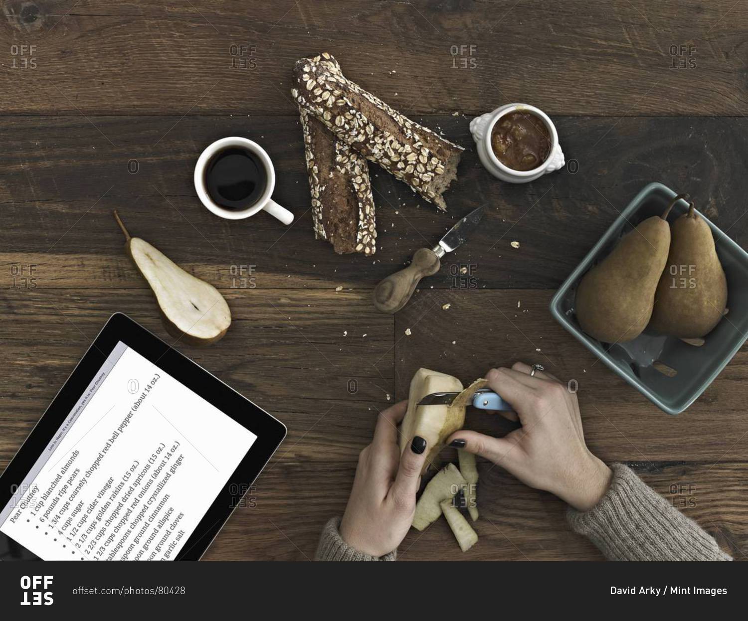A person using a peeling knife to peel a pear. A computer tablet device ...