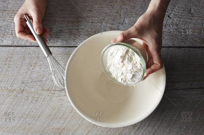 Top view of pouring flour from a small glass bowl into a larger white ...