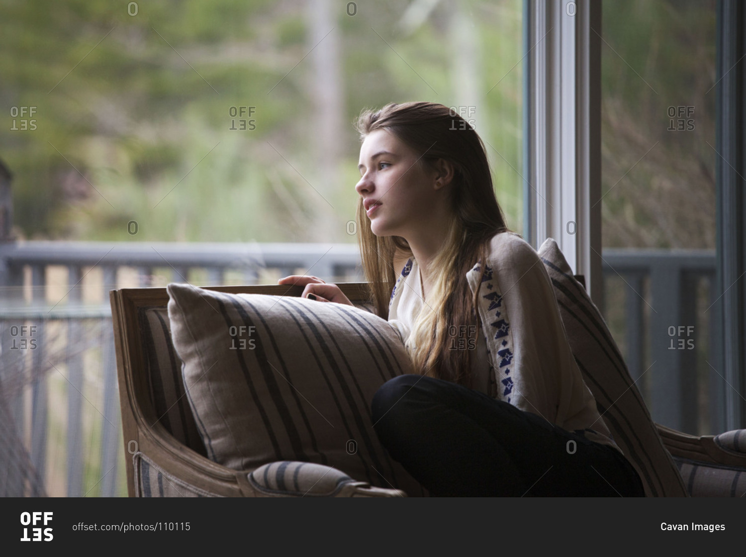 Teen girl looking out window on couch stock photo - OFFSET