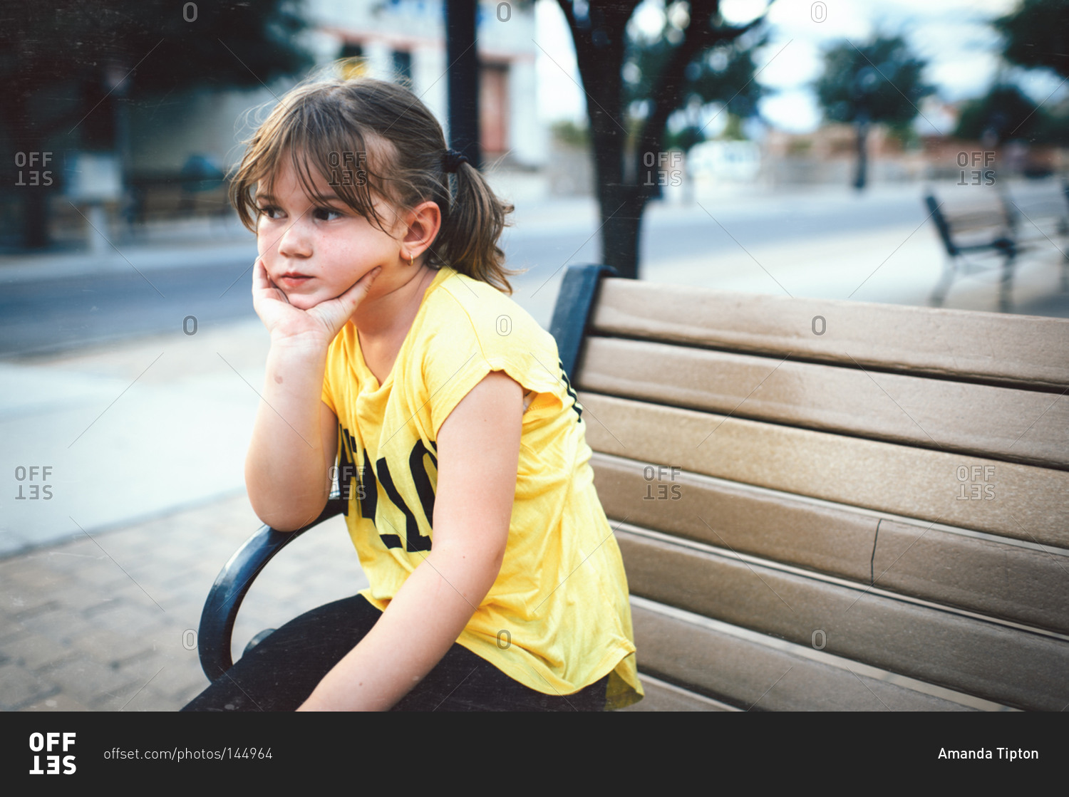 Bored little girl waiting on bench stock photo - OFFSET