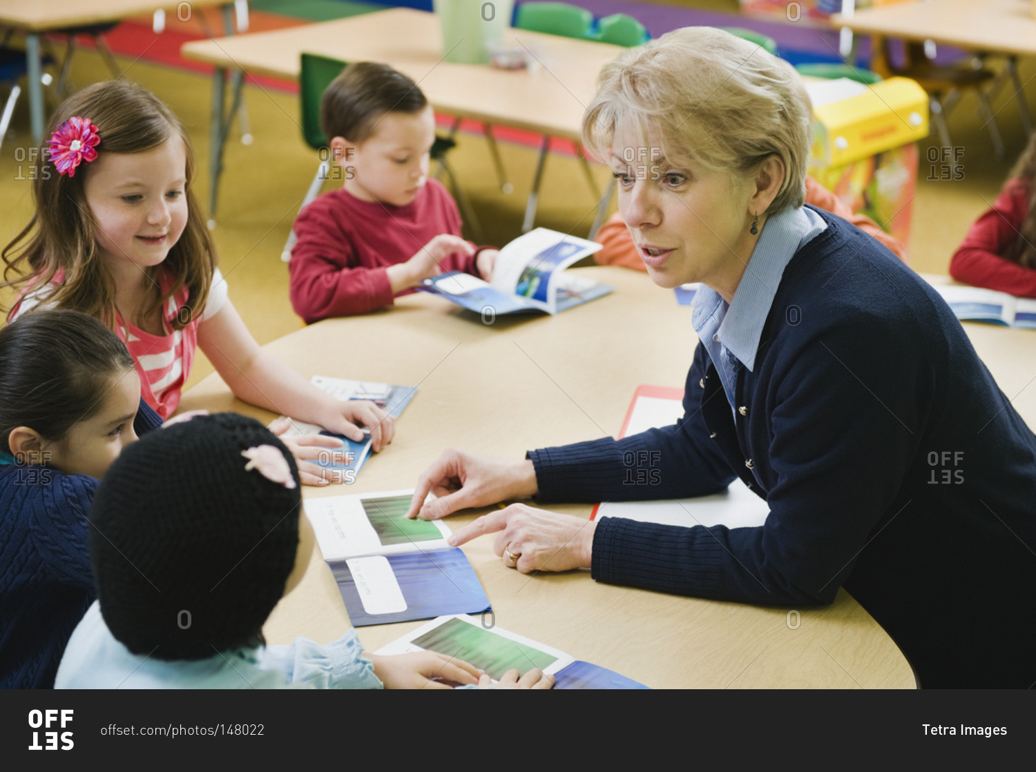 Kindergarten students sitting at table with teacher stock photo - OFFSET
