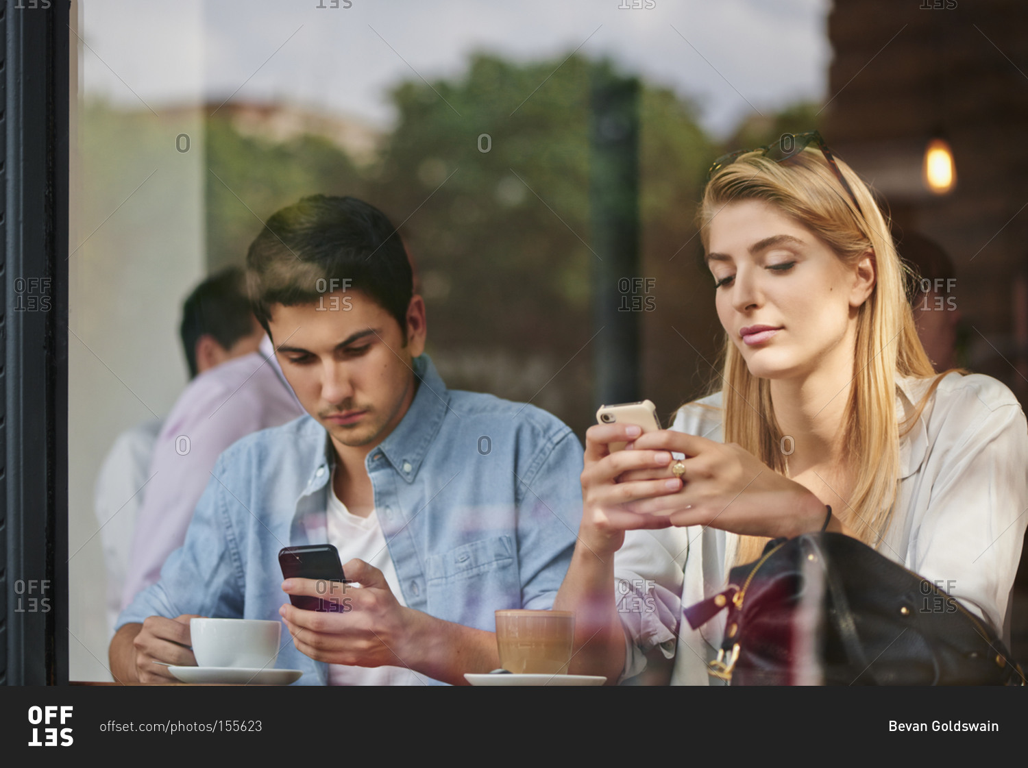 Two people in cafe window on their phones stock photo - OFFSET