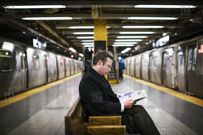 Man sitting reading magazine in subway station - Stock Image - Everypixel
