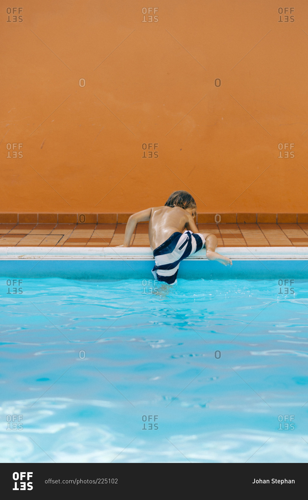 A young boy climbs into a pool stock photo - OFFSET