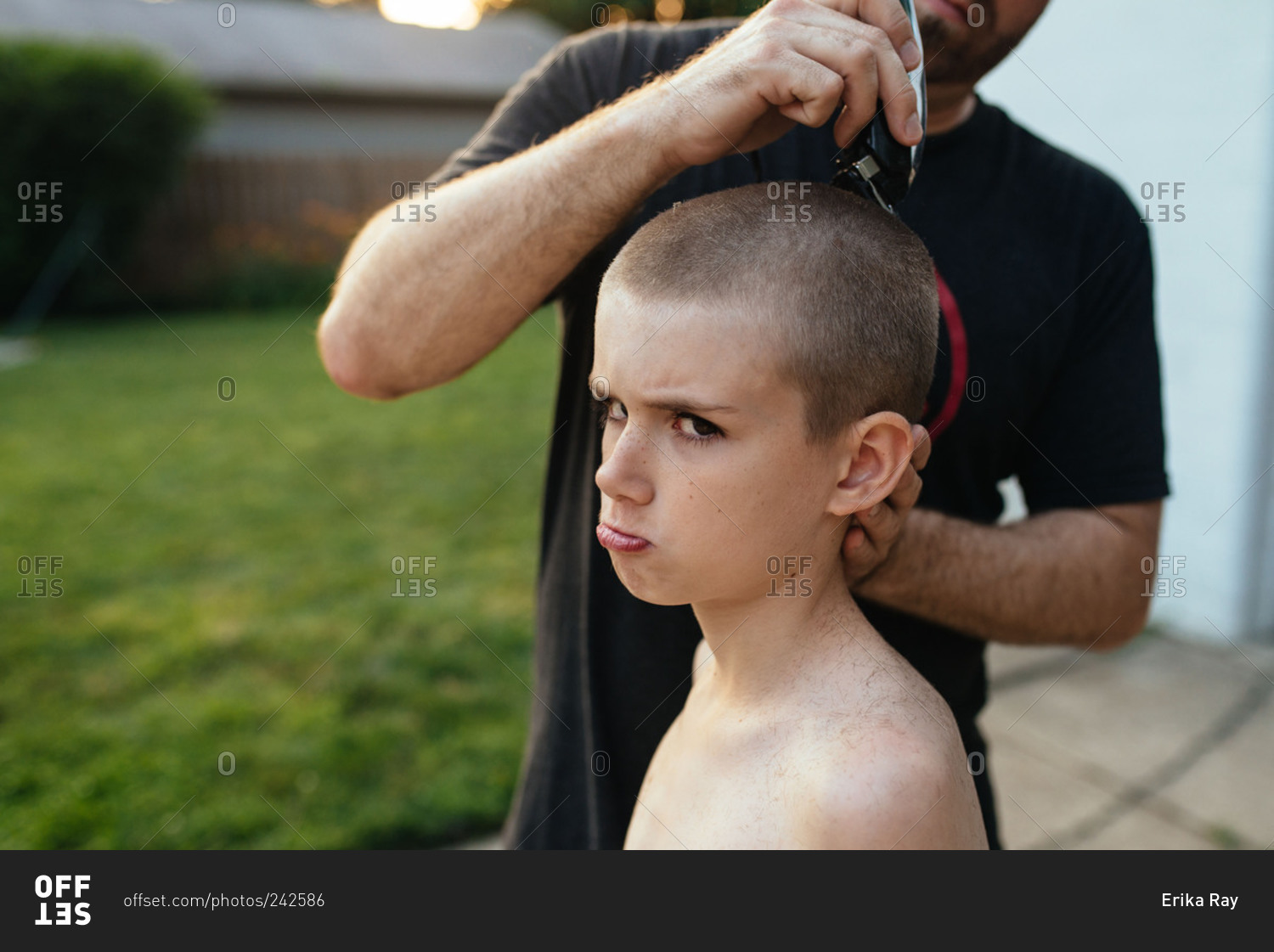 Man shaving boy's head outside stock photo - OFFSET