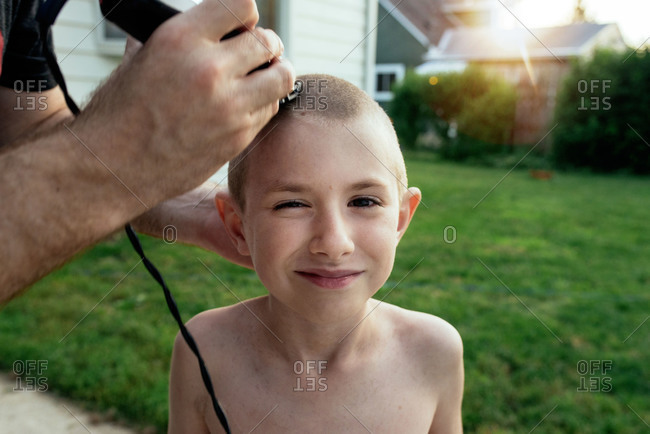 Boy getting his hair buzzed outdoors stock photo - OFFSET