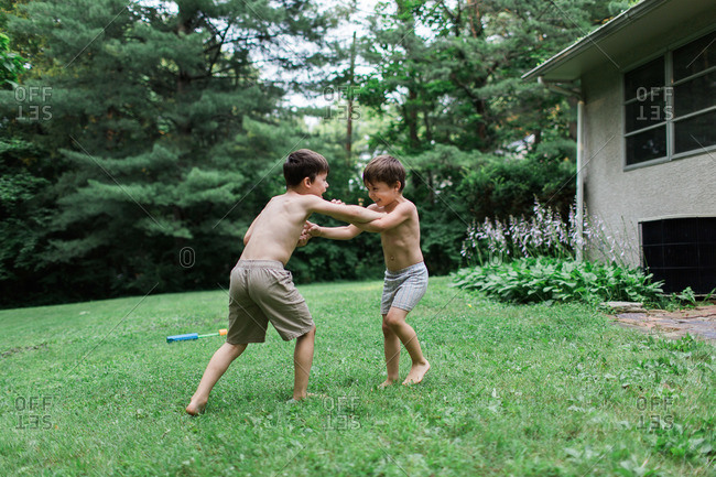 Two young brothers wrestle in their backyard stock photo - OFFSET