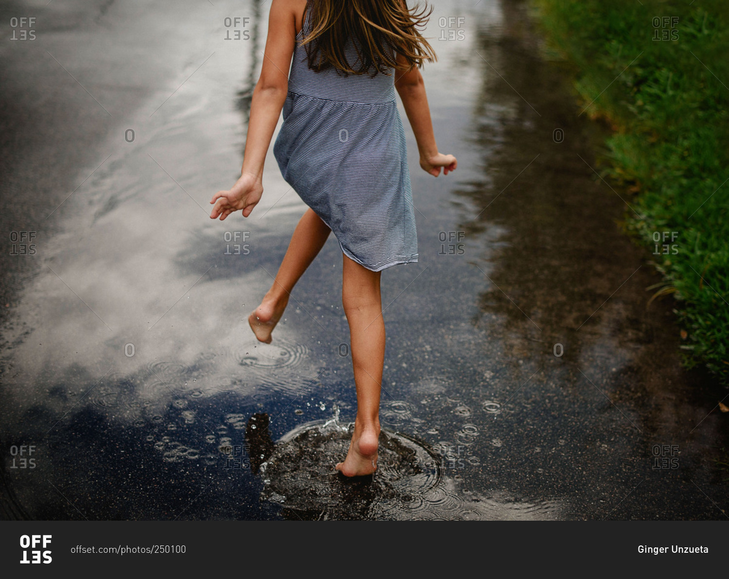 Girl running barefoot through a puddle on the street stock photo - OFFSET