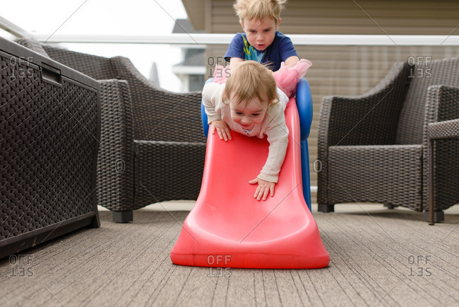 A boy pushes his little sister down a slide head first stock photo - OFFSET