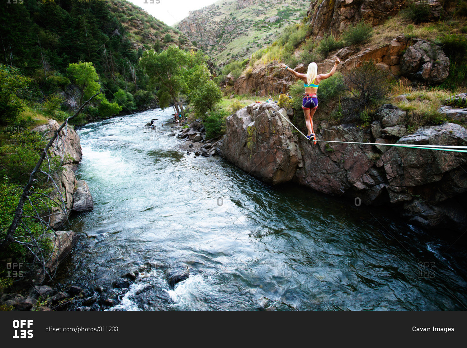 Woman walking on a tightrope over a river stock photo - OFFSET