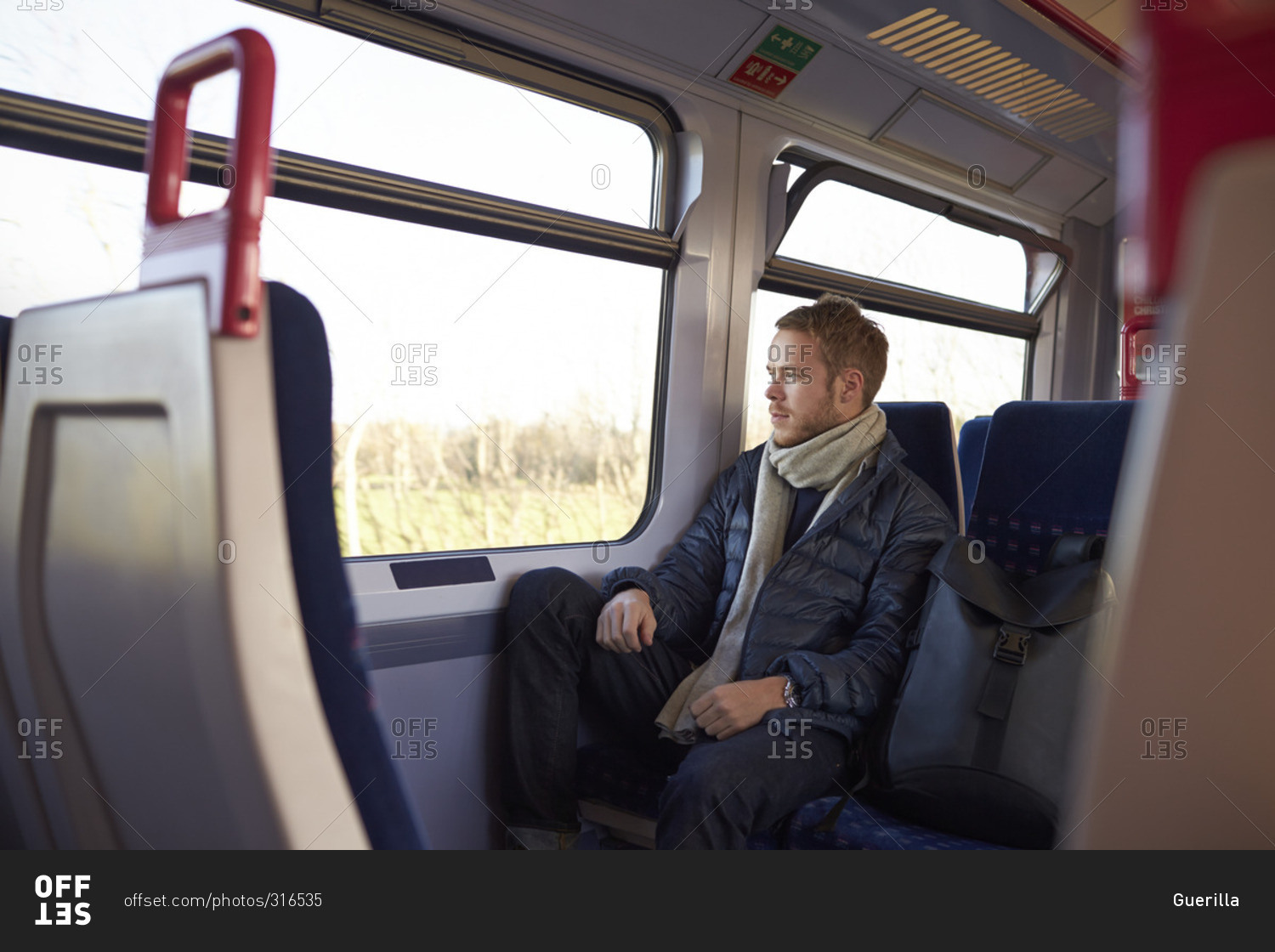 Young Man Sitting In Train Carriage On Railway Journey stock photo - OFFSET