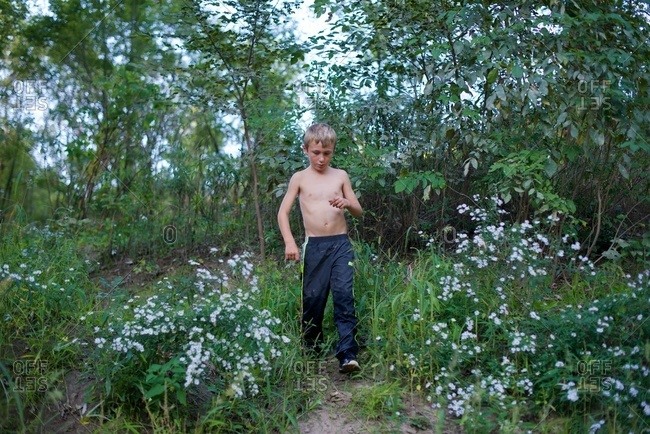 Shirtless boy walking on forest trail stock photo - OFFSET