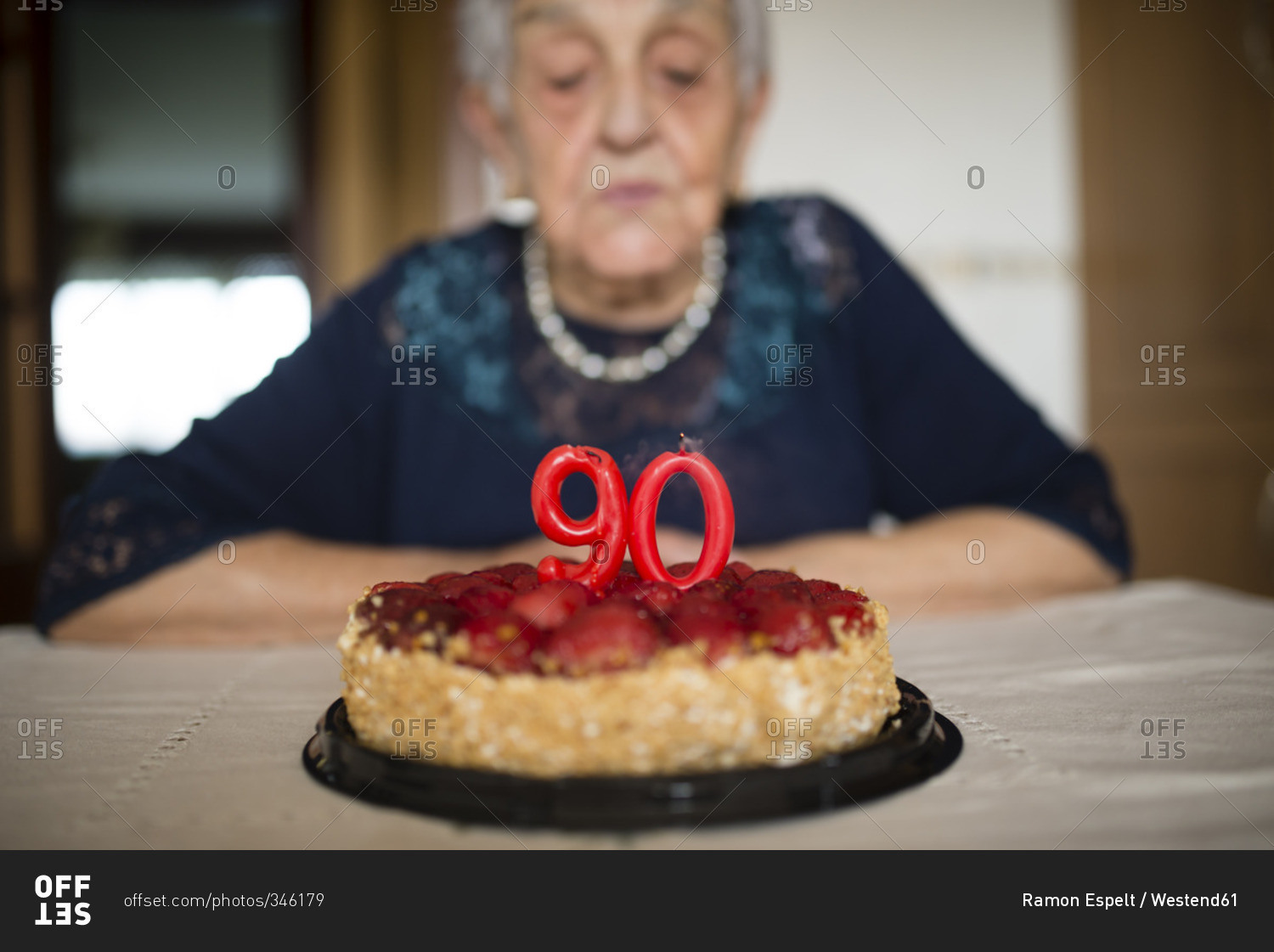Portrait Of Senior Woman Blowing Out The Candles On Her Birthday Cake