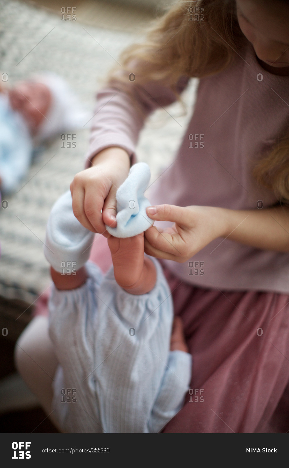 Little girl changing baby doll's clothes stock photo - OFFSET