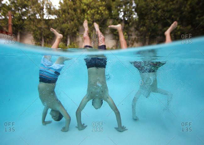 Waterline view of boys doing handstands in pool stock photo - OFFSET