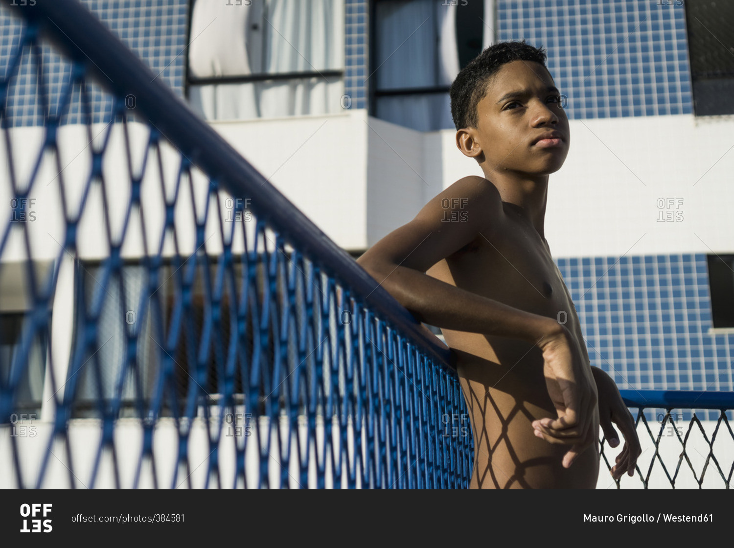 Bare chested teenage boy leaning on fence stock photo - OFFSET