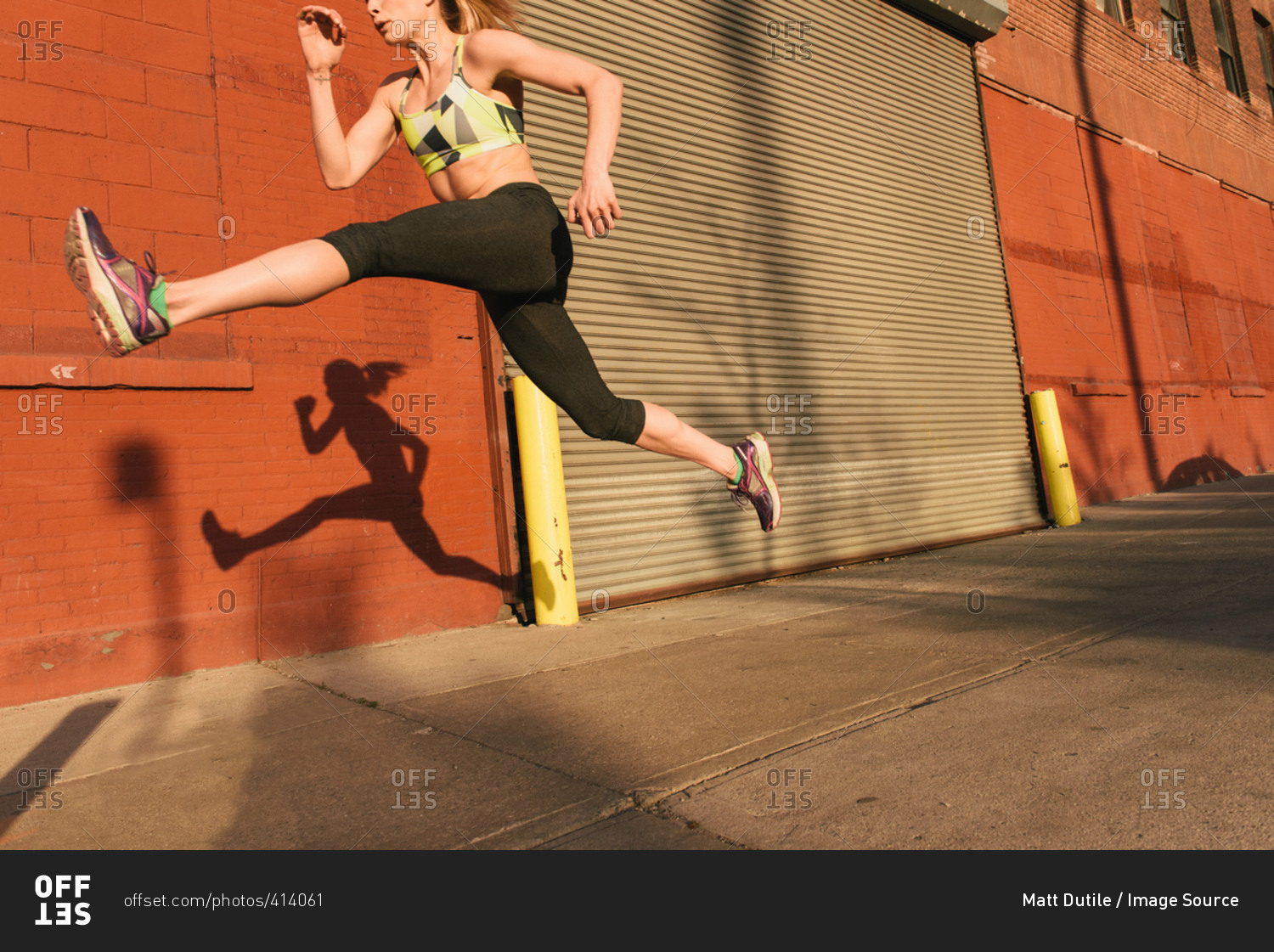 Young woman exercising outdoors, leaping through air, shadow beside her ...