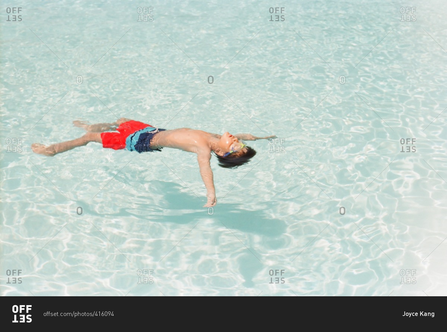 Young boy floating on back in swimming pool stock photo - OFFSET
