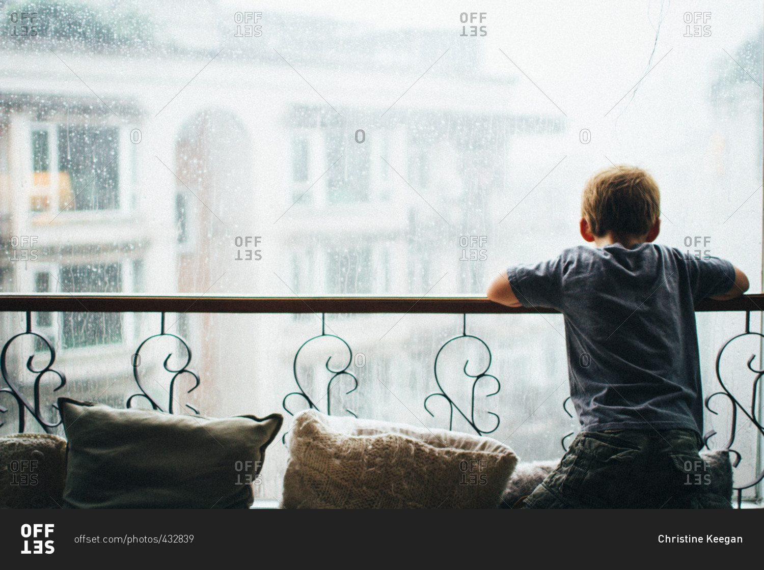 Boy looking out rainy city window stock photo - OFFSET