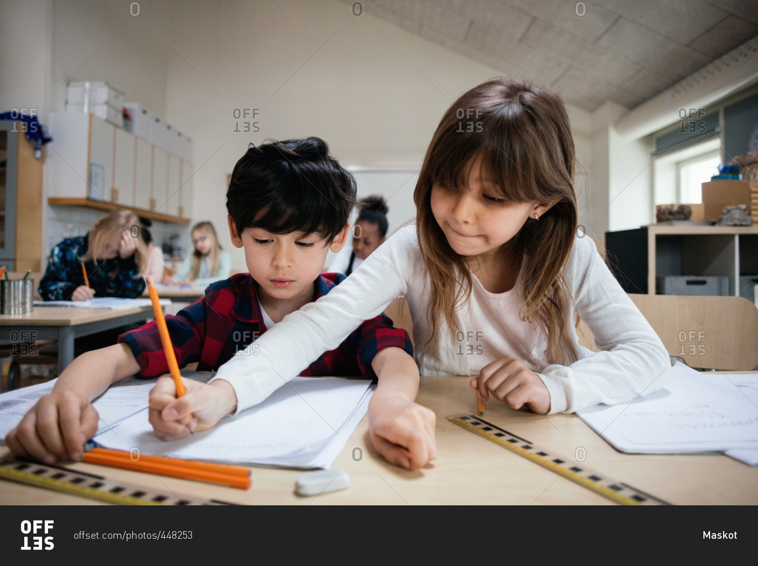Female friend helping student while studying at desk in classroom stock ...