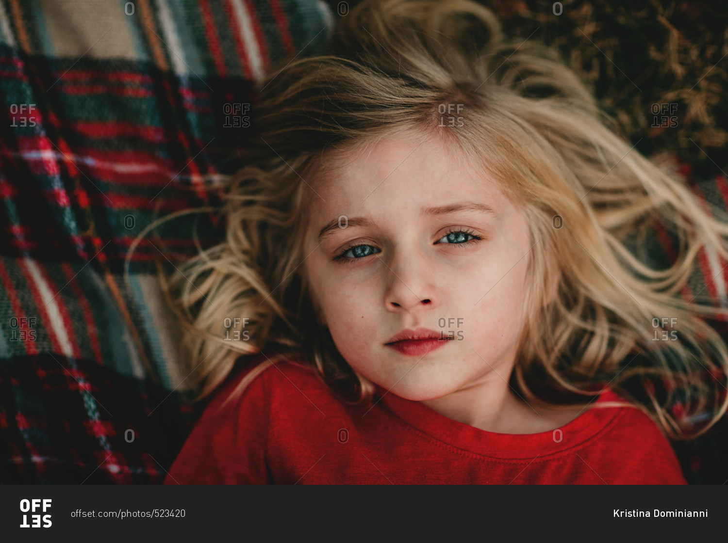 Little girl lying outside on a plaid blanket stock photo - OFFSET