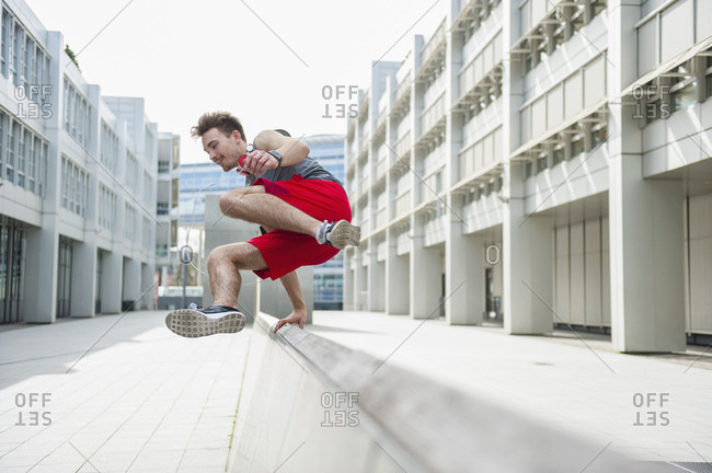 Young man wearing sports clothing, jumping over wall - Stock Image ...
