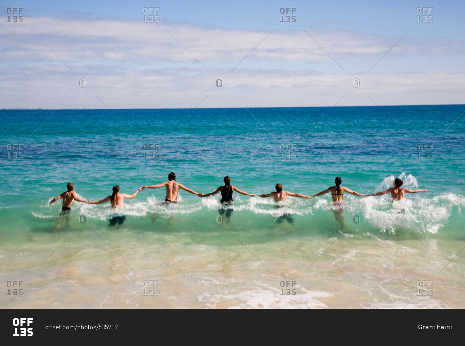 Many people holding hands wading in the ocean as waves break around ...