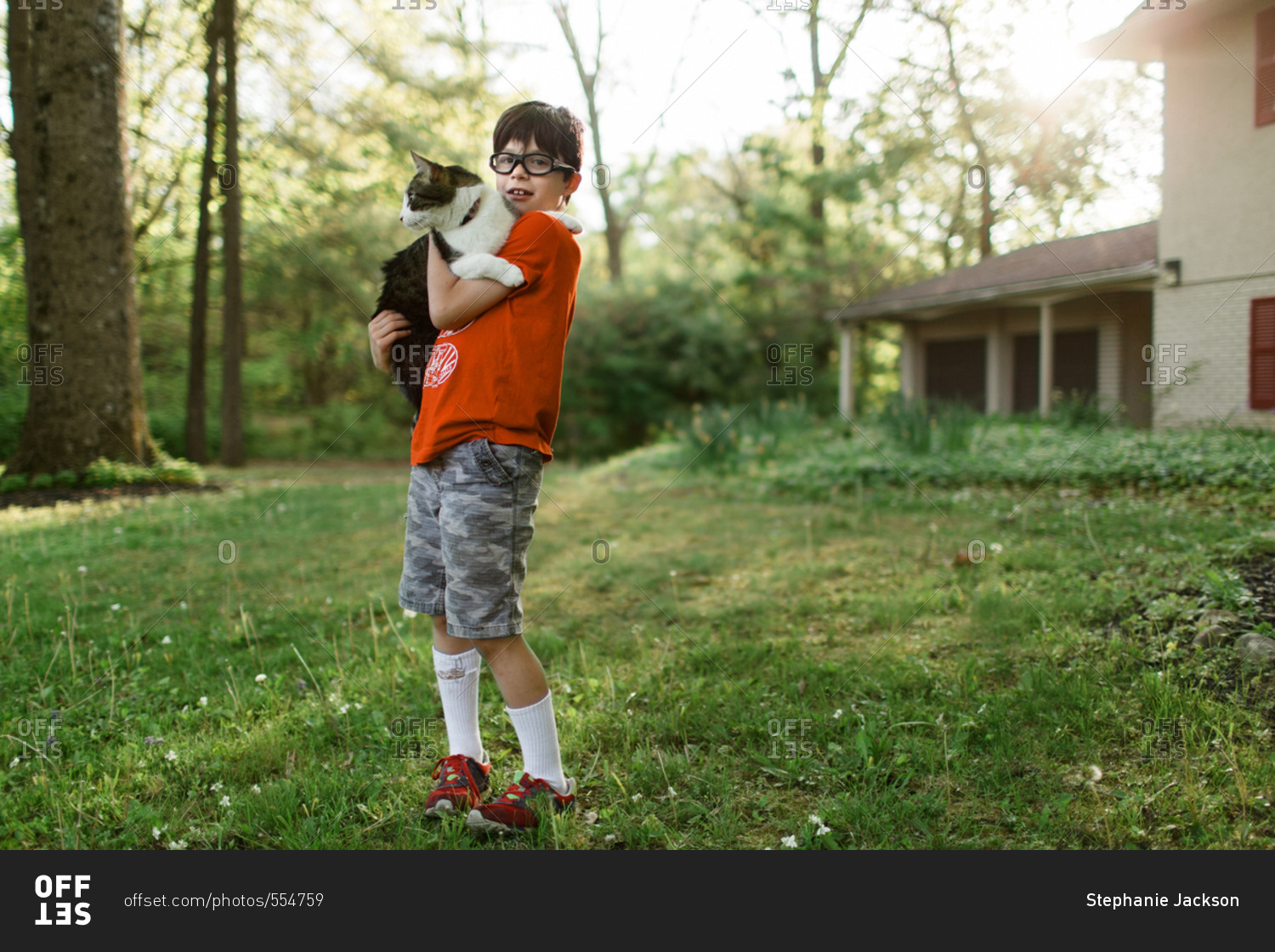 Boy in front yard holding a cat stock photo - OFFSET