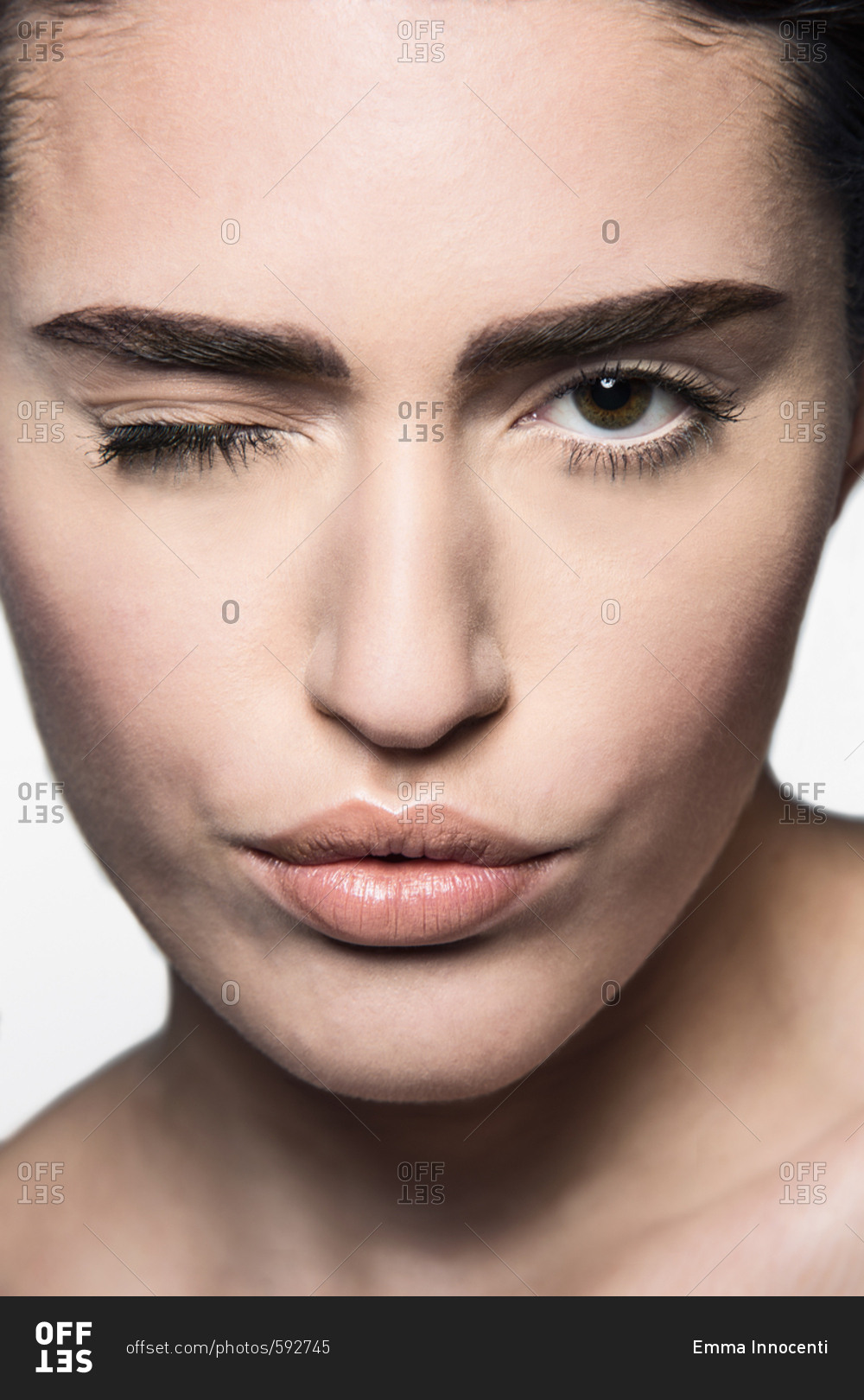 Close up of young woman's face winking at camera stock photo - OFFSET