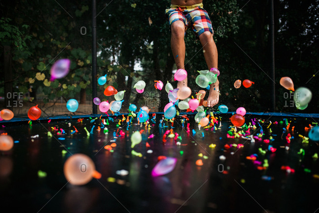 Boy jumping on trampoline with water balloons stock photo - OFFSET