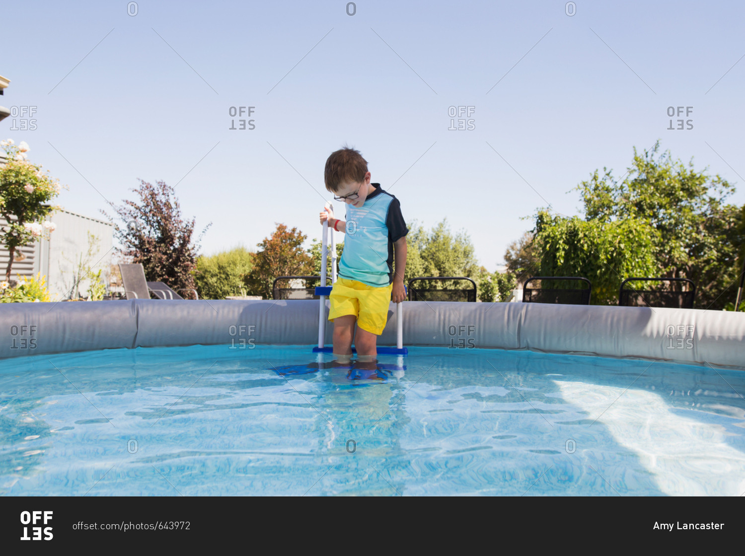 Boy climbing down ladder into swimming pool stock photo - OFFSET