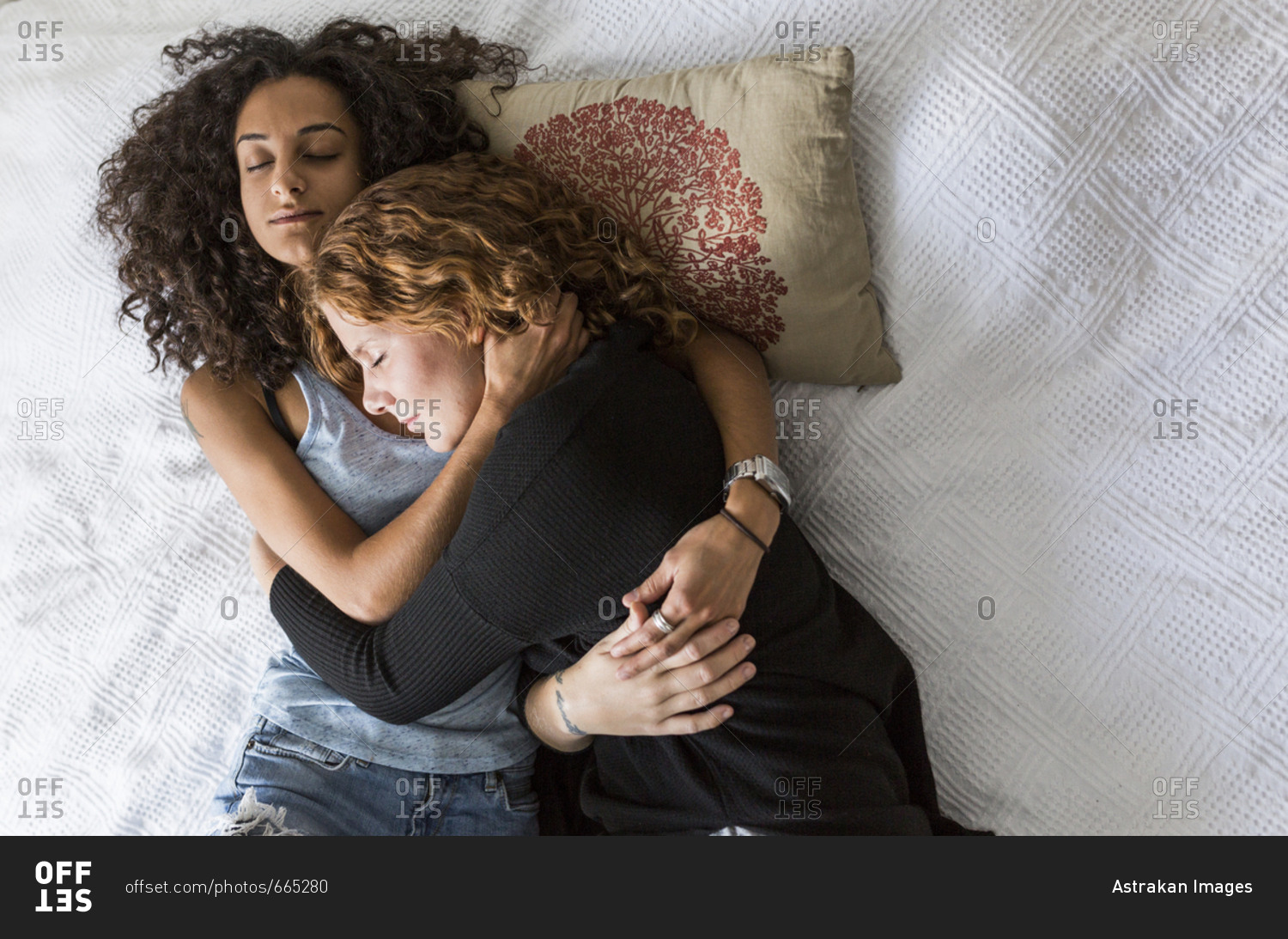 Two women lying down on bed and cuddling stock photo - OFFSET