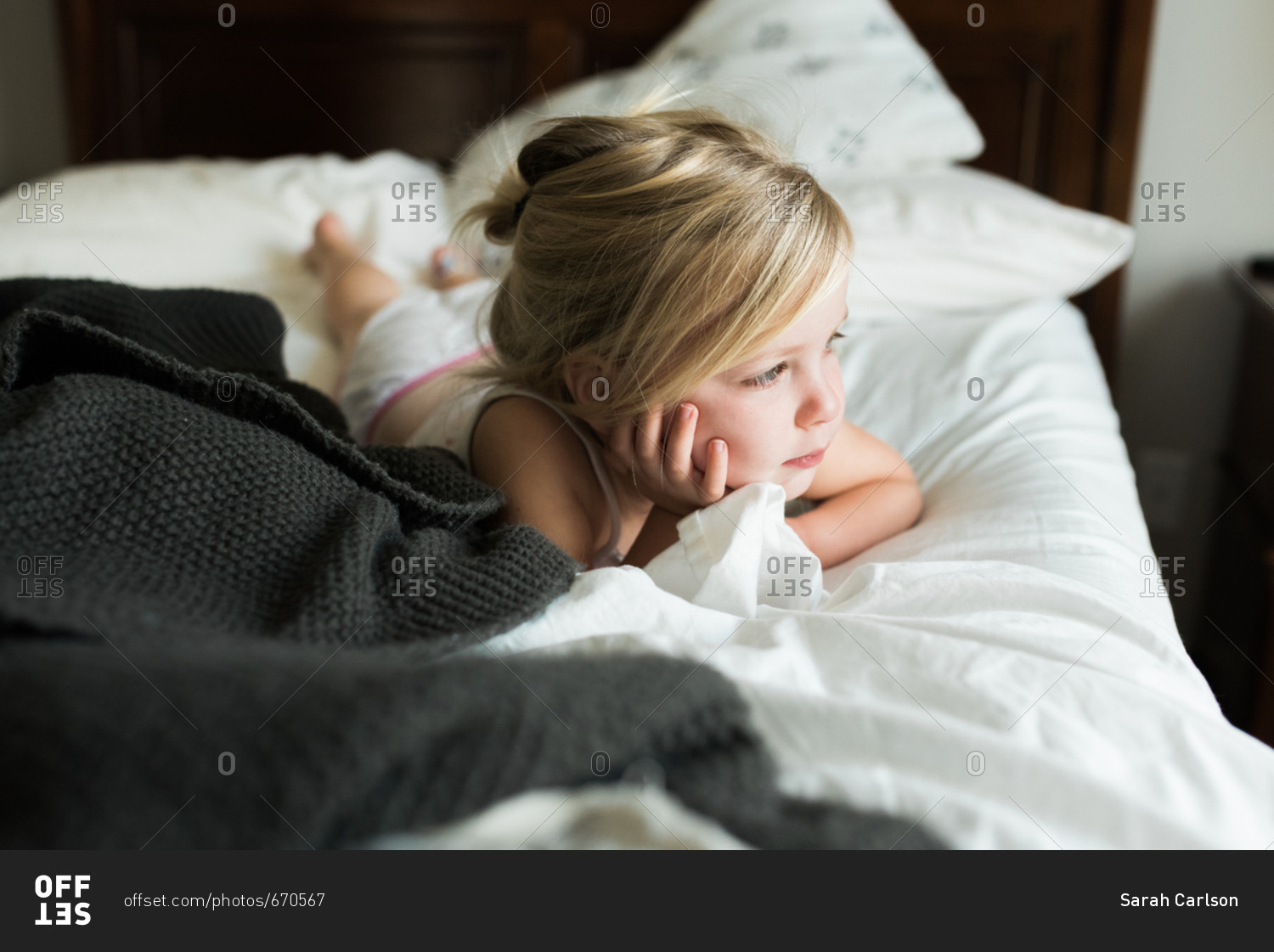 Little girl lying on big bed with chin in hand deep in thought stock ...