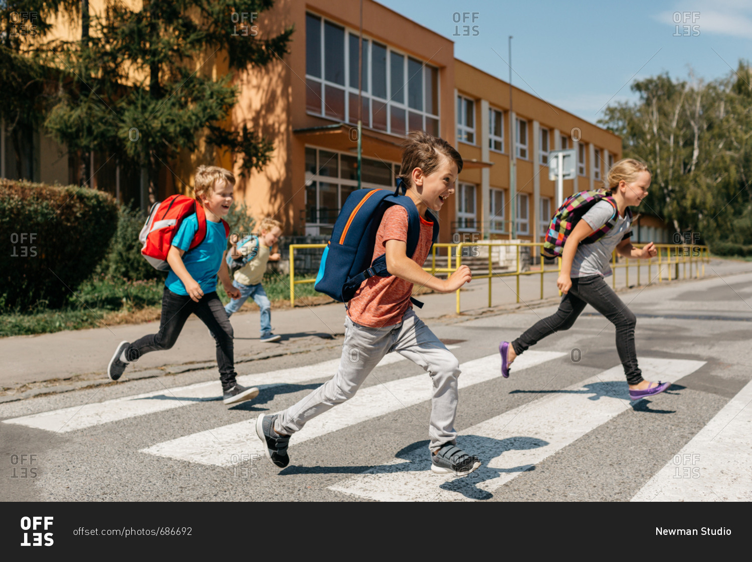 A group of laughing classmates rushing out of school crossing road ...