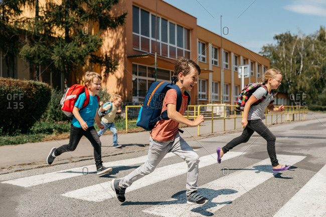 A group of laughing classmates rushing out of school crossing road ...