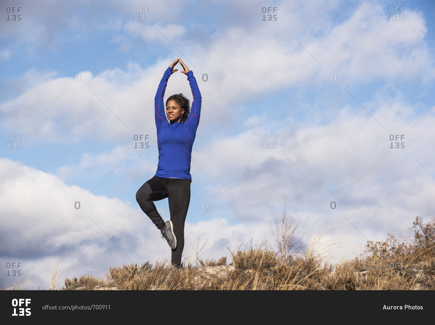 Young female yoga practitioner standing against clouds on one leg with ...