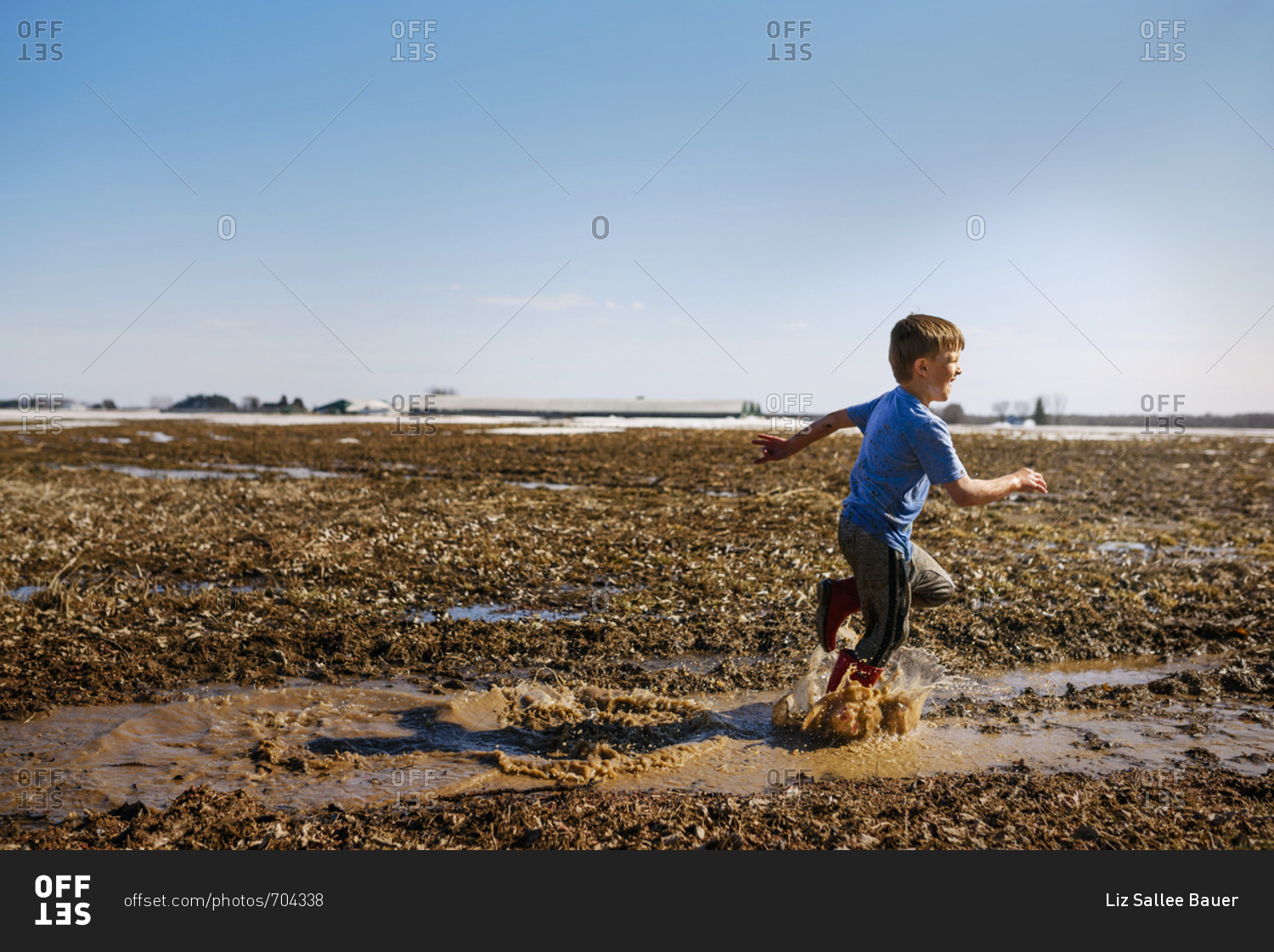 A young boy jumping in mud puddles in a field stock photo - OFFSET