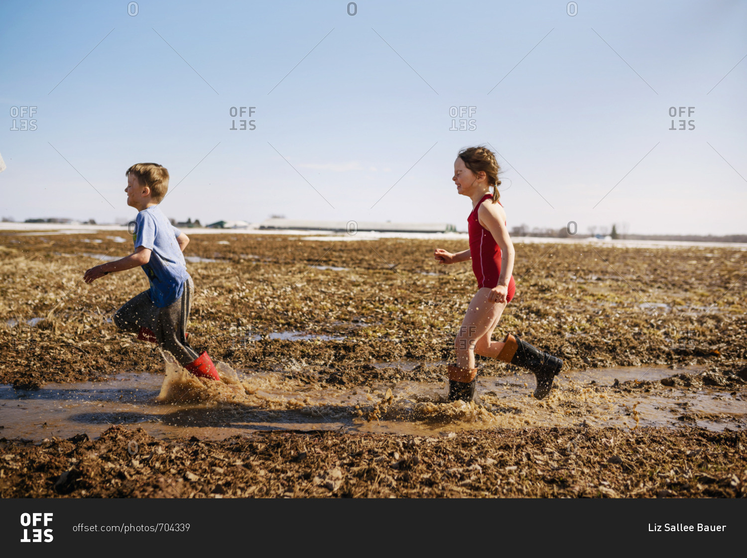 Two young kids jumping in mud puddles in a field stock photo - OFFSET