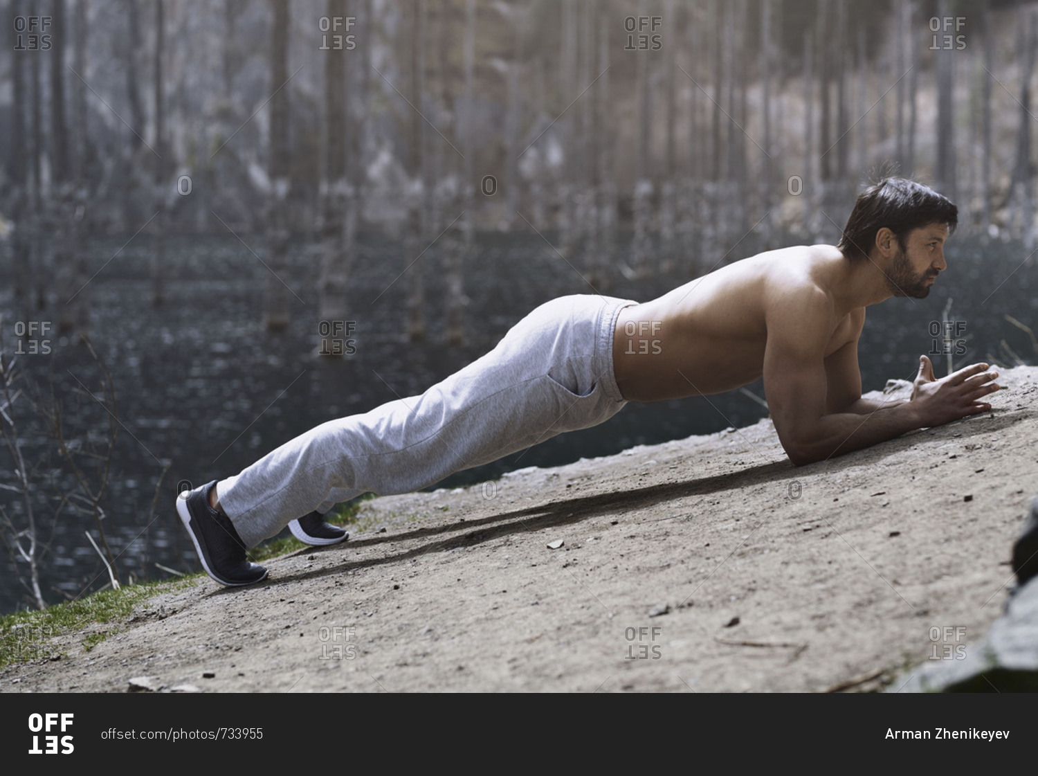 Man doing plank exercise at mountain lake stock photo - OFFSET