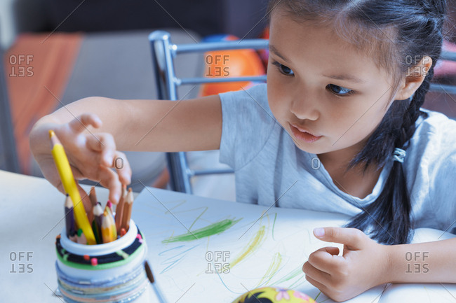 Girl picking up colored pencil from the jar stock photo - OFFSET