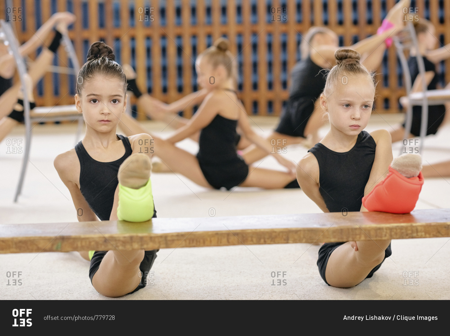 Portrait Of Two Young Gymnasts In Black Uniform Doing Splits On Bench