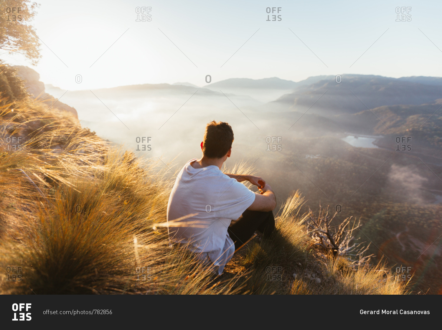 Man sitting on top of hill watching sunrise stock photo - OFFSET