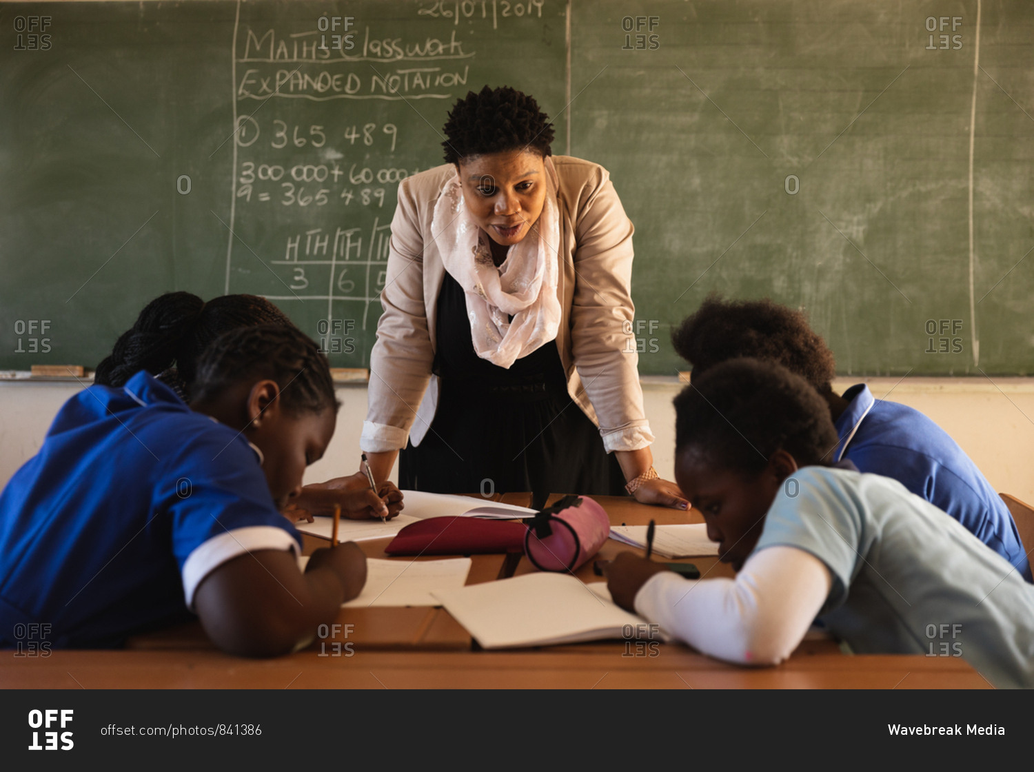 African female school teacher standing at the blackboard and leaning ...