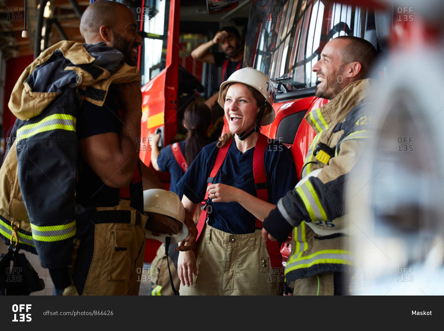 Happy firefighters talking while standing against fire engine at fire ...