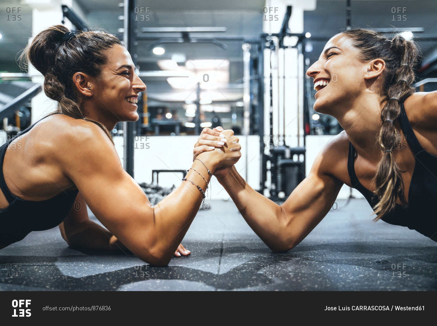 Happy female twins in good shape doing arm wrestling challenge in a gym ...