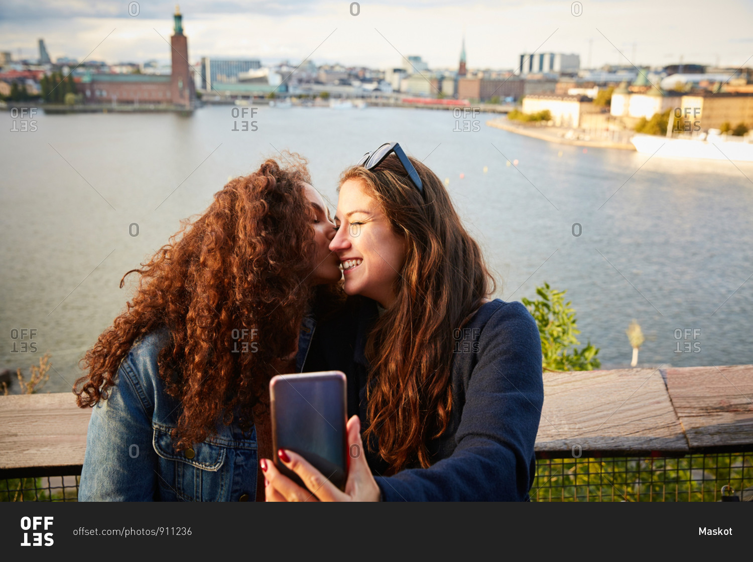 Smiling Lesbian Couple Kissing While Taking Selfie With Mobile Phone Against Cityscape Stock