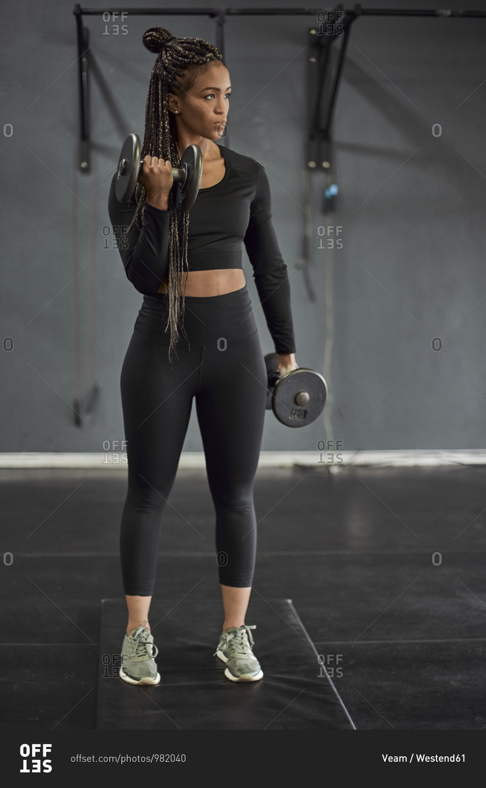 Confident female athlete with braided hair lifting dumbbells in health ...