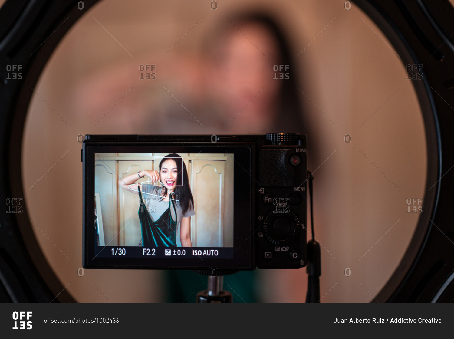 Cheerful young Asian female blogger seen on camera display recording content for fashion channel ...